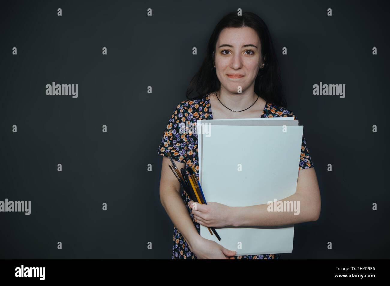 young woman artist looking into camera with album and painting tools in ...