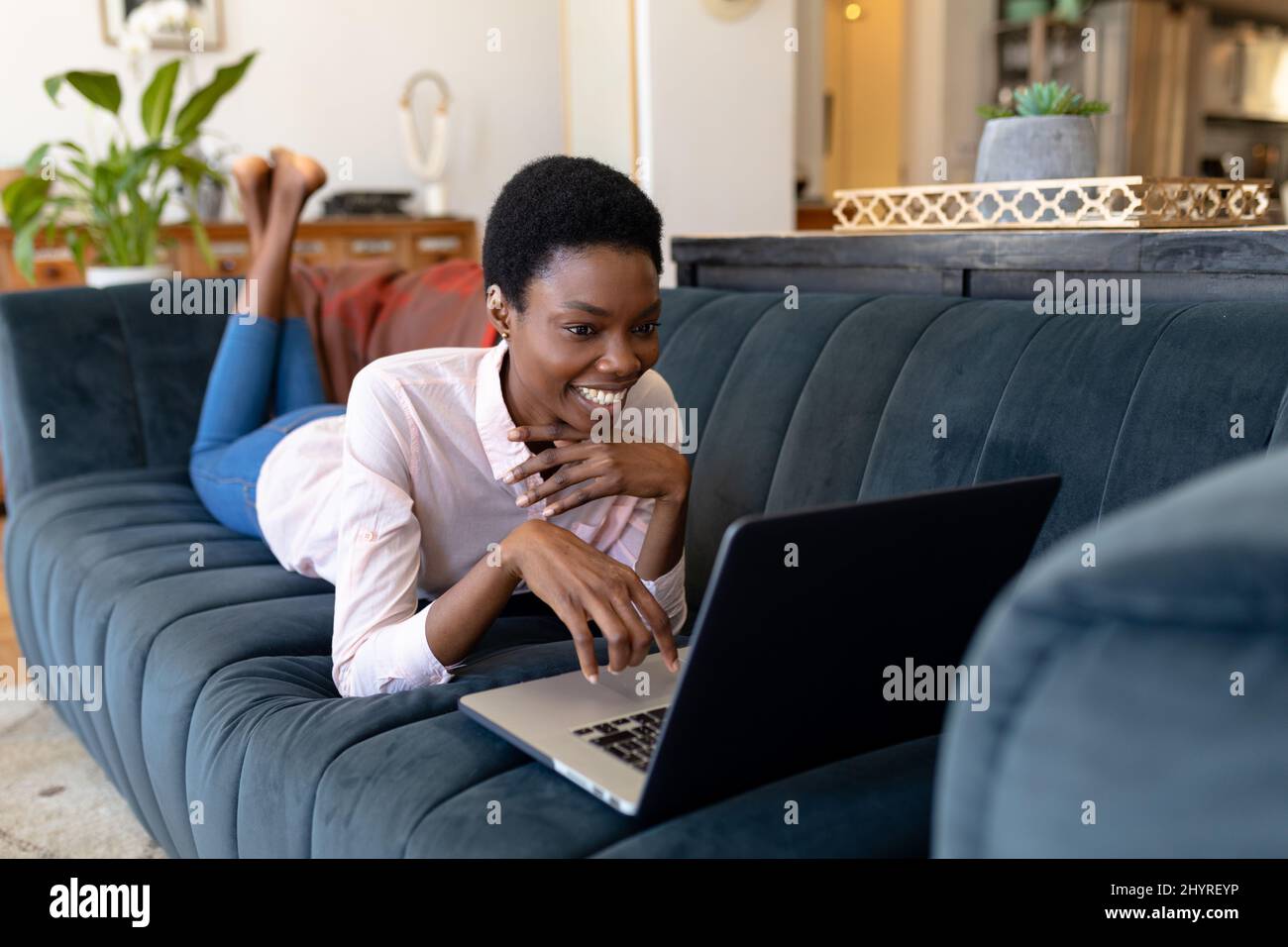 Happy african american woman lying on sofa while using laptop in living ...