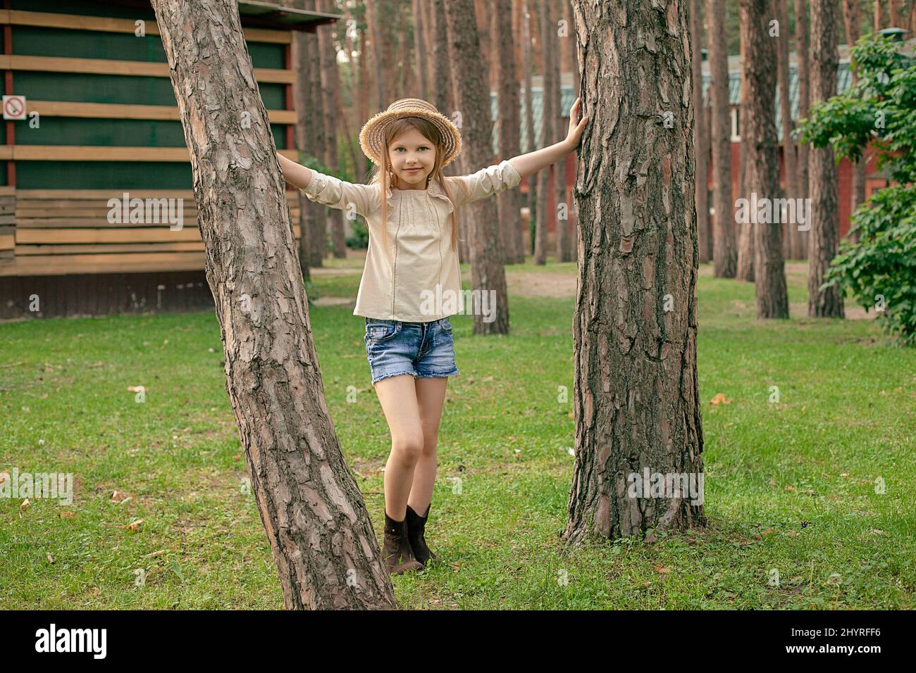 Smiling tween girl standing touching on two trees in green summer ...