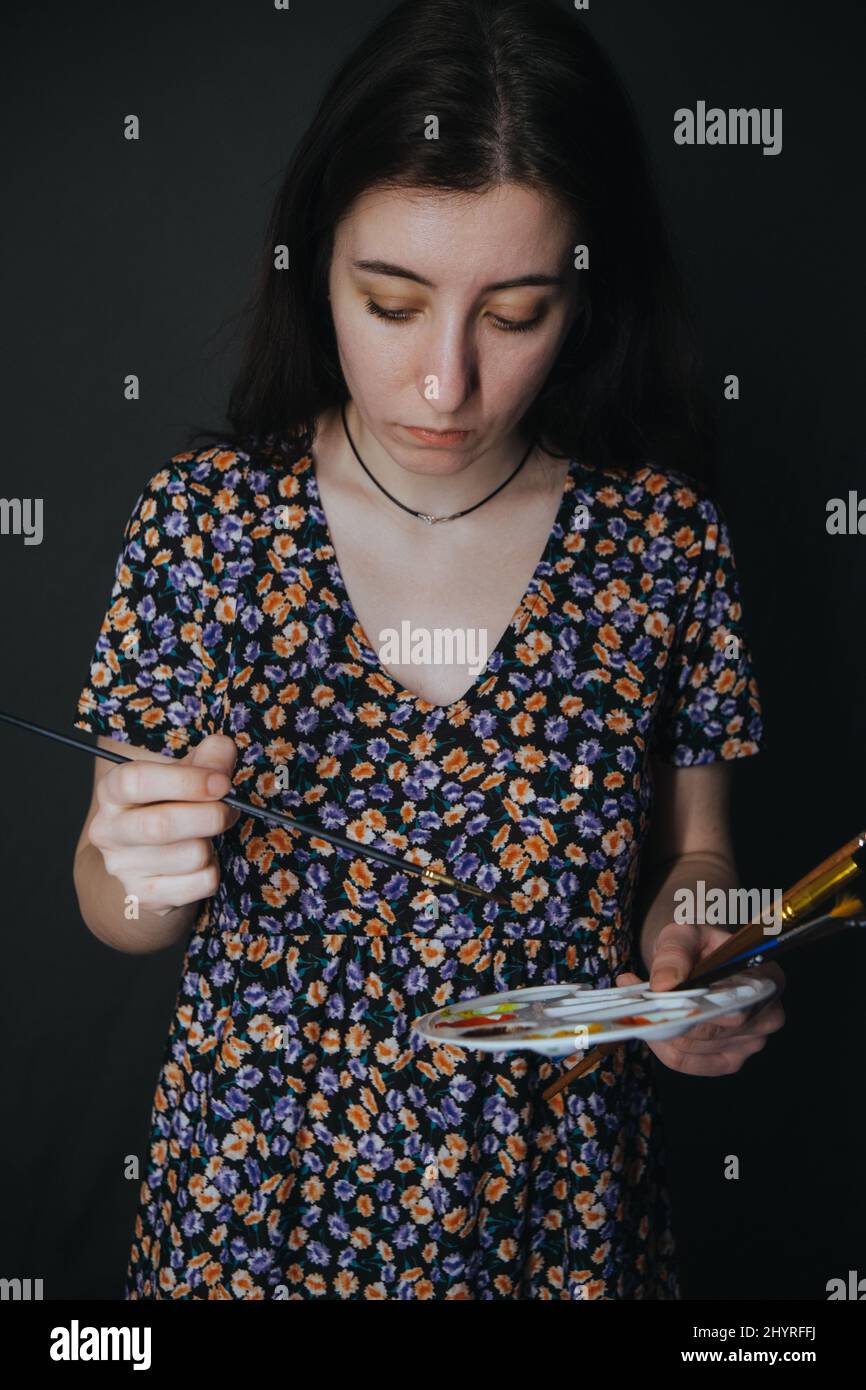 young woman artist looking into camera with album and painting tools in ...