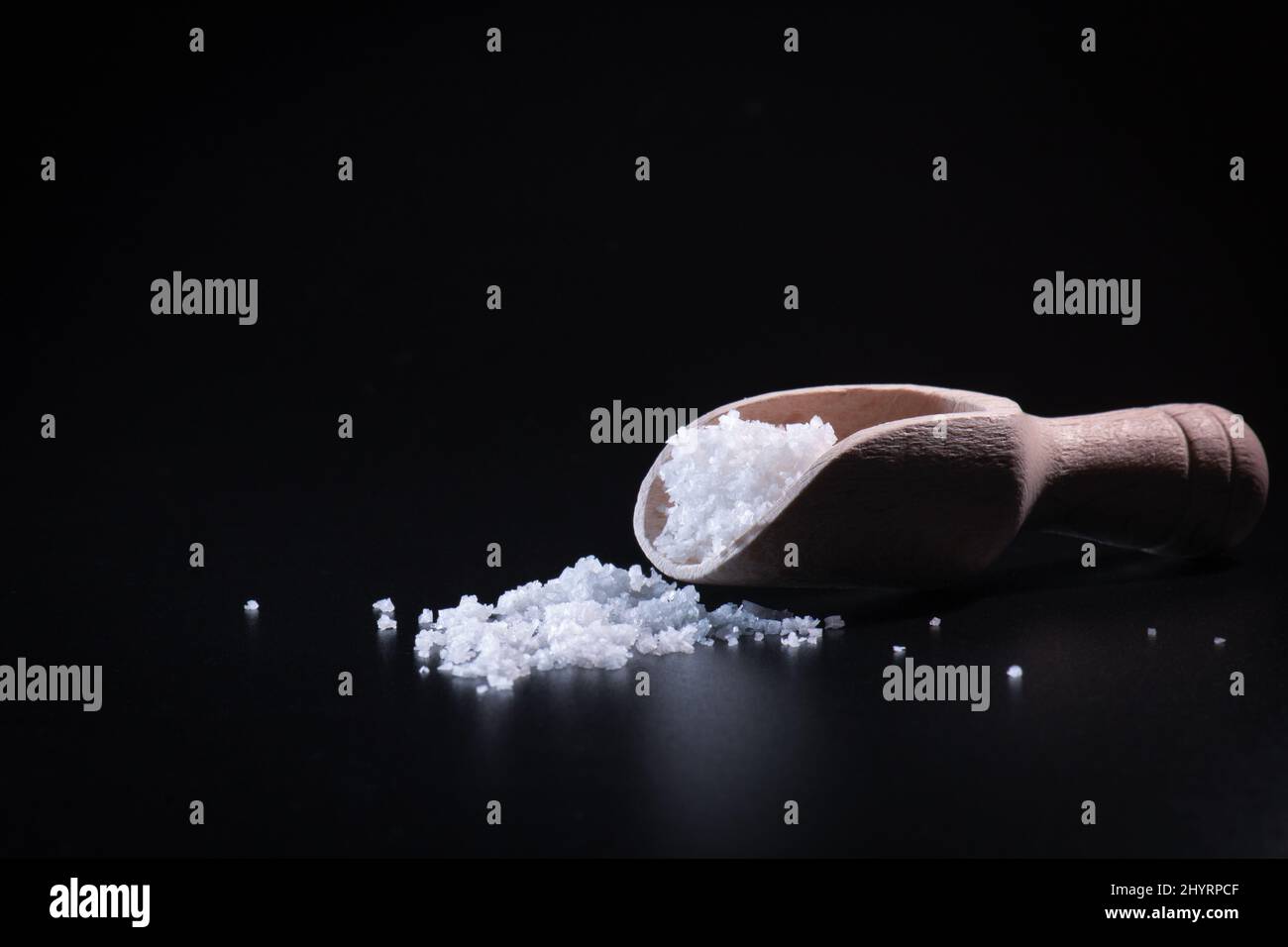 Close-up shot of a wooden spoon full of salt isolated on a black ...