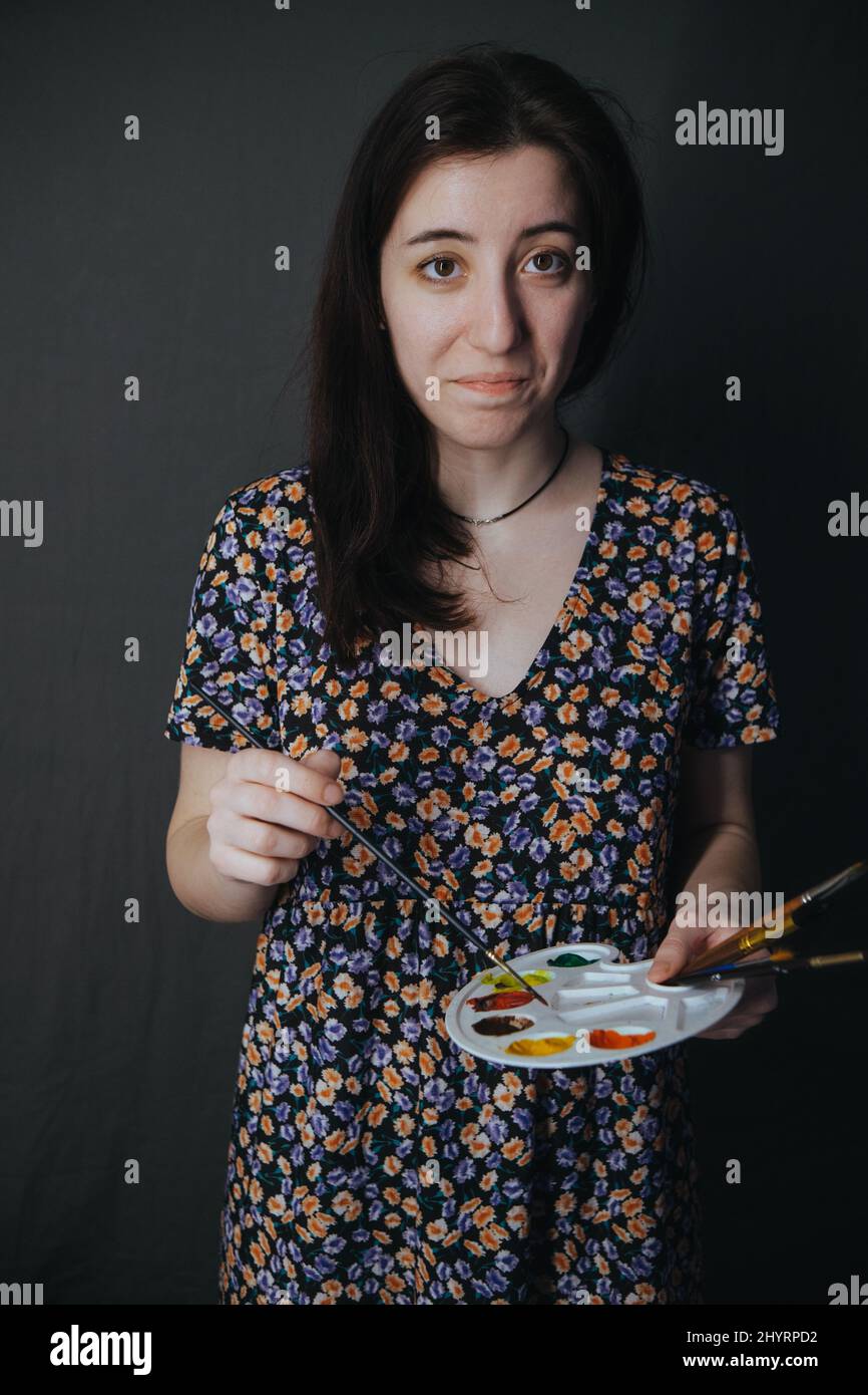young woman artist looking into camera with album and painting tools in ...