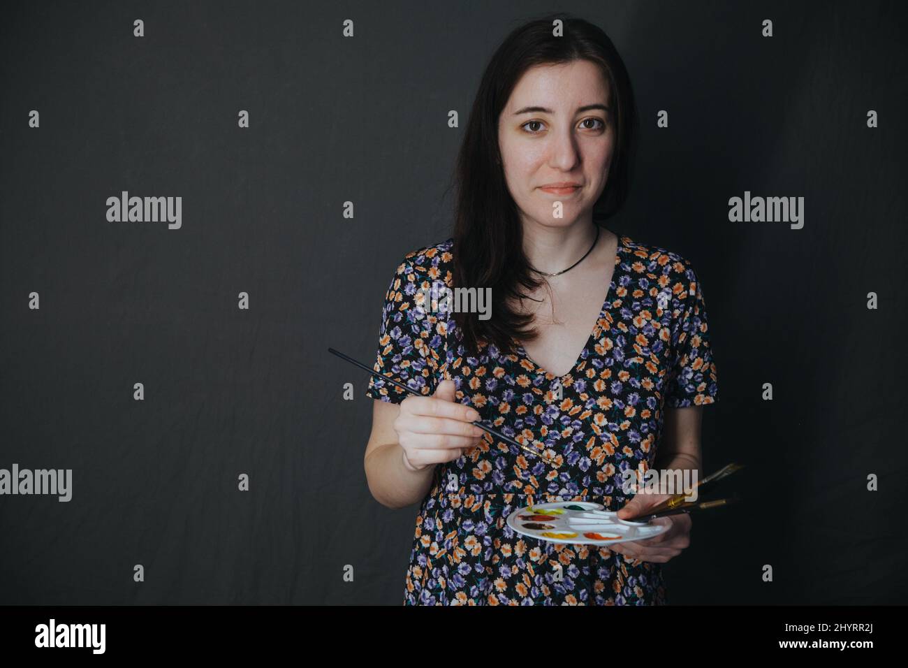 young woman artist looking into camera with album and painting tools in ...