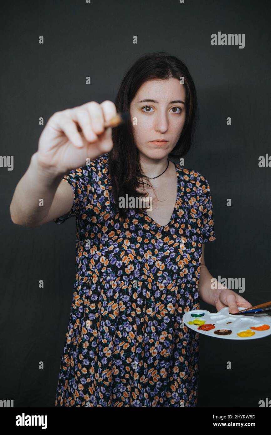 young woman artist looking into camera with album and painting tools in ...