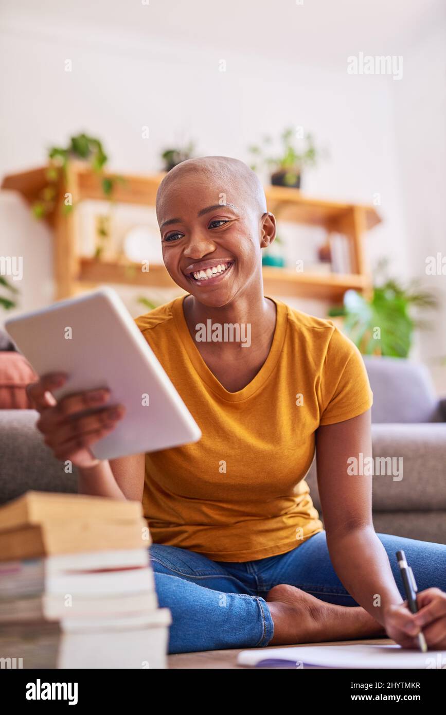 A young student sits on the floor studying taking notes from her tablet ...