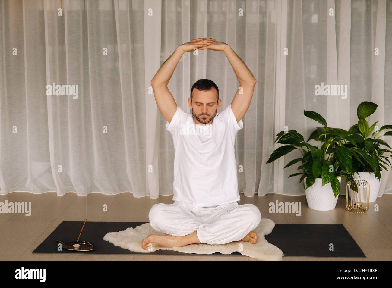a man in white sportswear is doing yoga with a fitness room. the ...