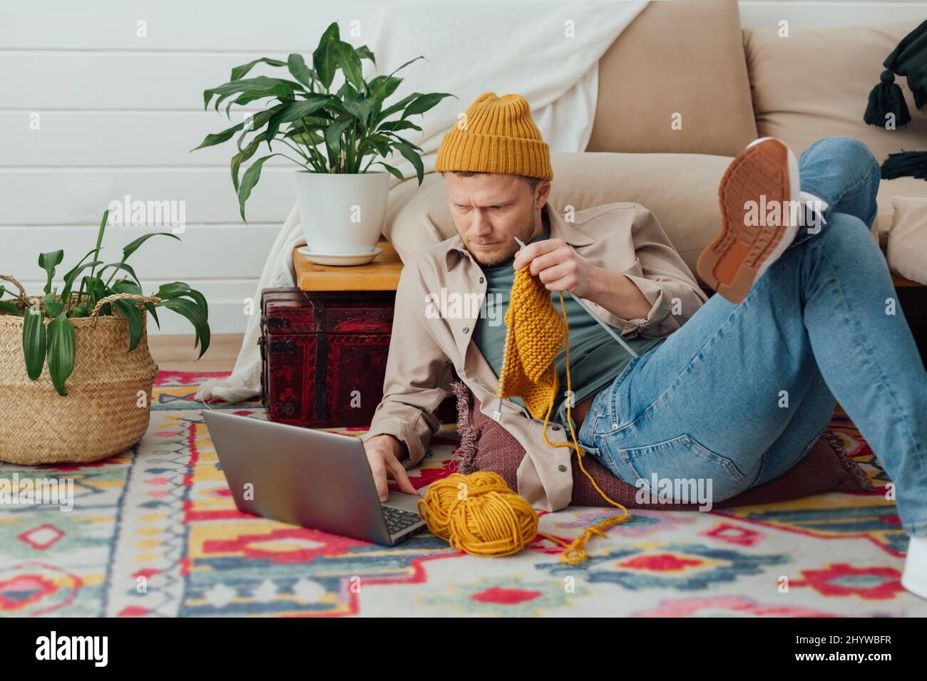Young serious man looking at laptop. Man learning new hobby, knitting ...