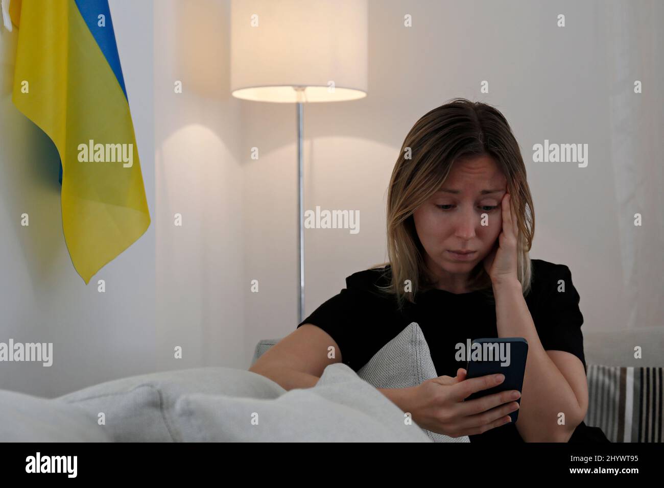 Young anxious woman with cried out eyes reading the news about Ukraine ...
