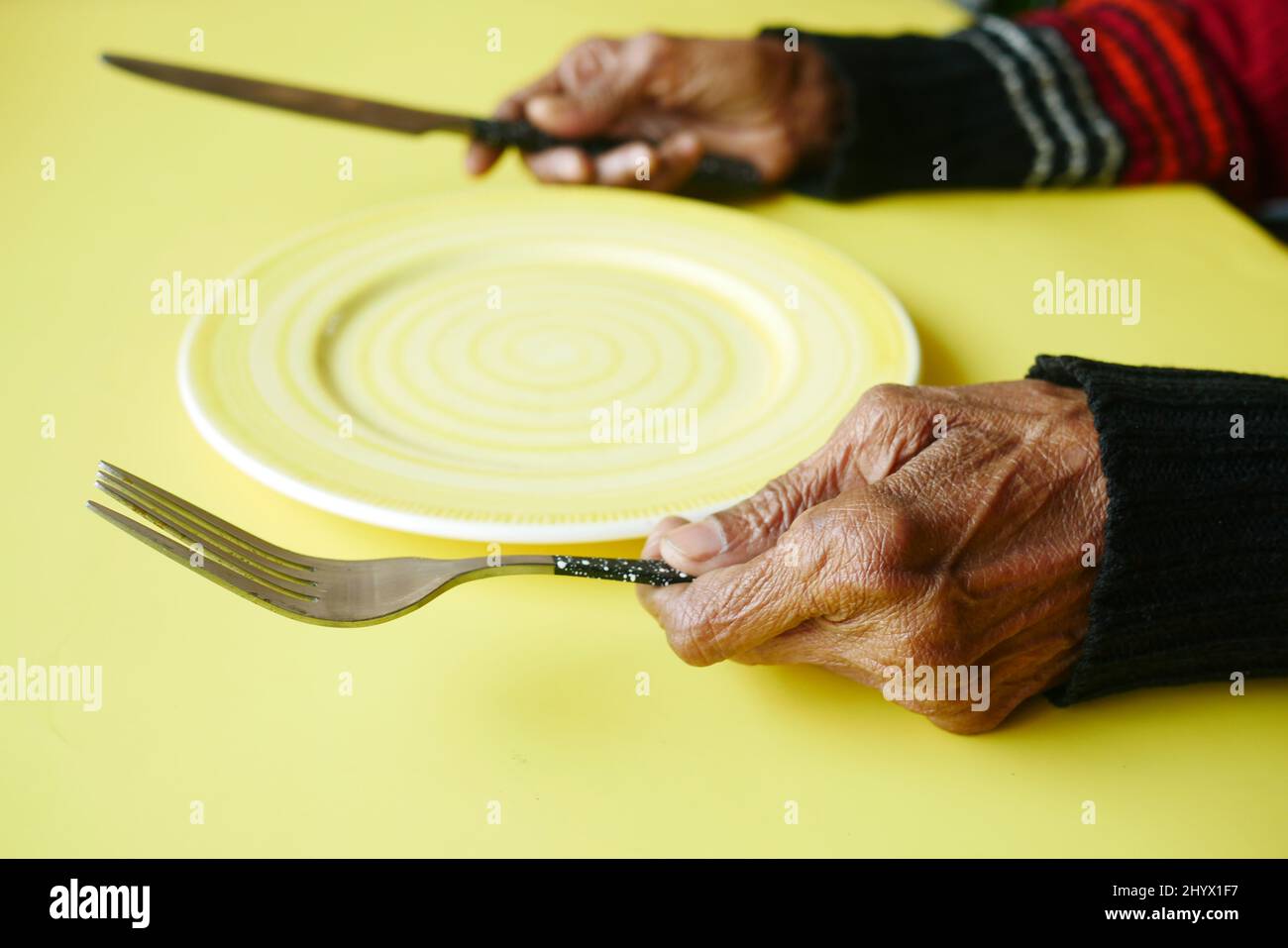senior women holding cutlery with empty plate on yellow background ...