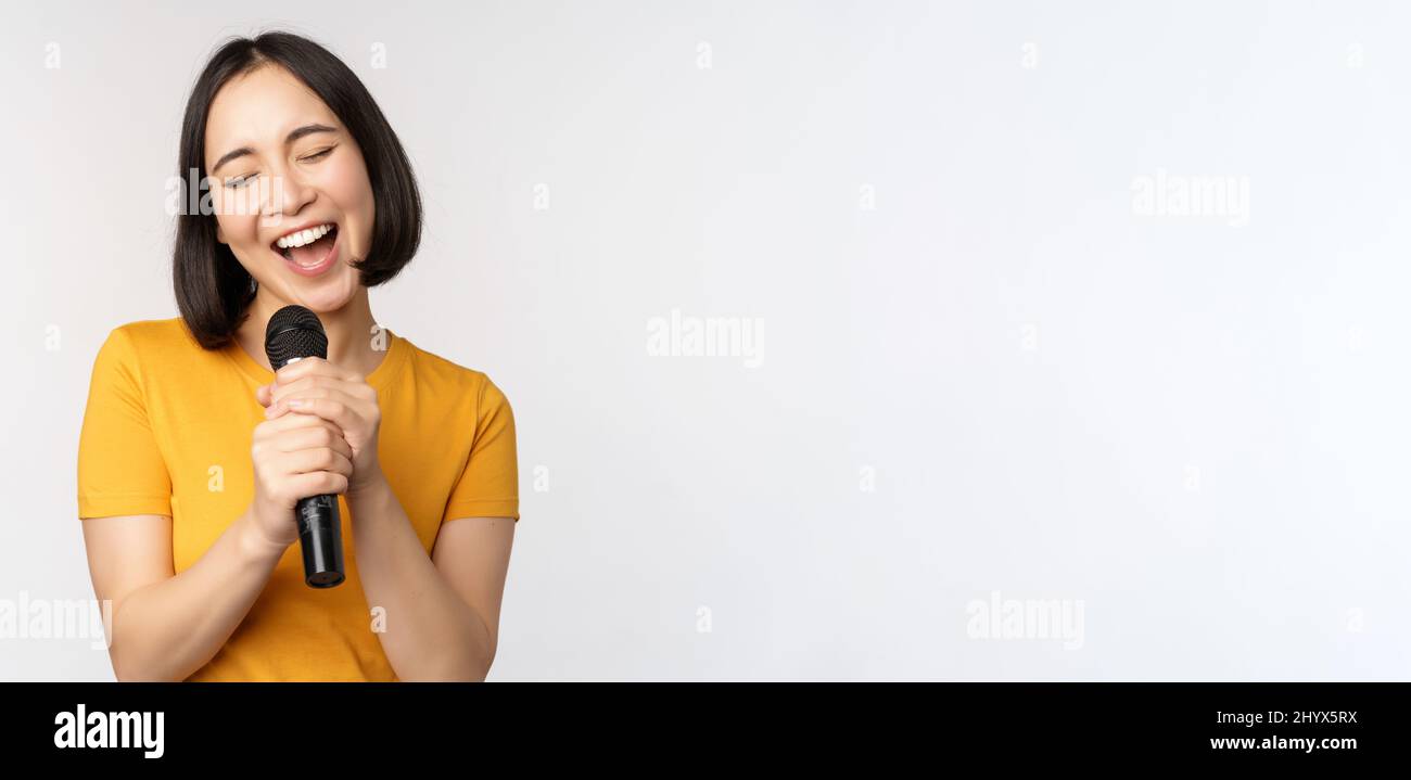 Happy asian girl singing and having fun, holding microphone at karaoke ...