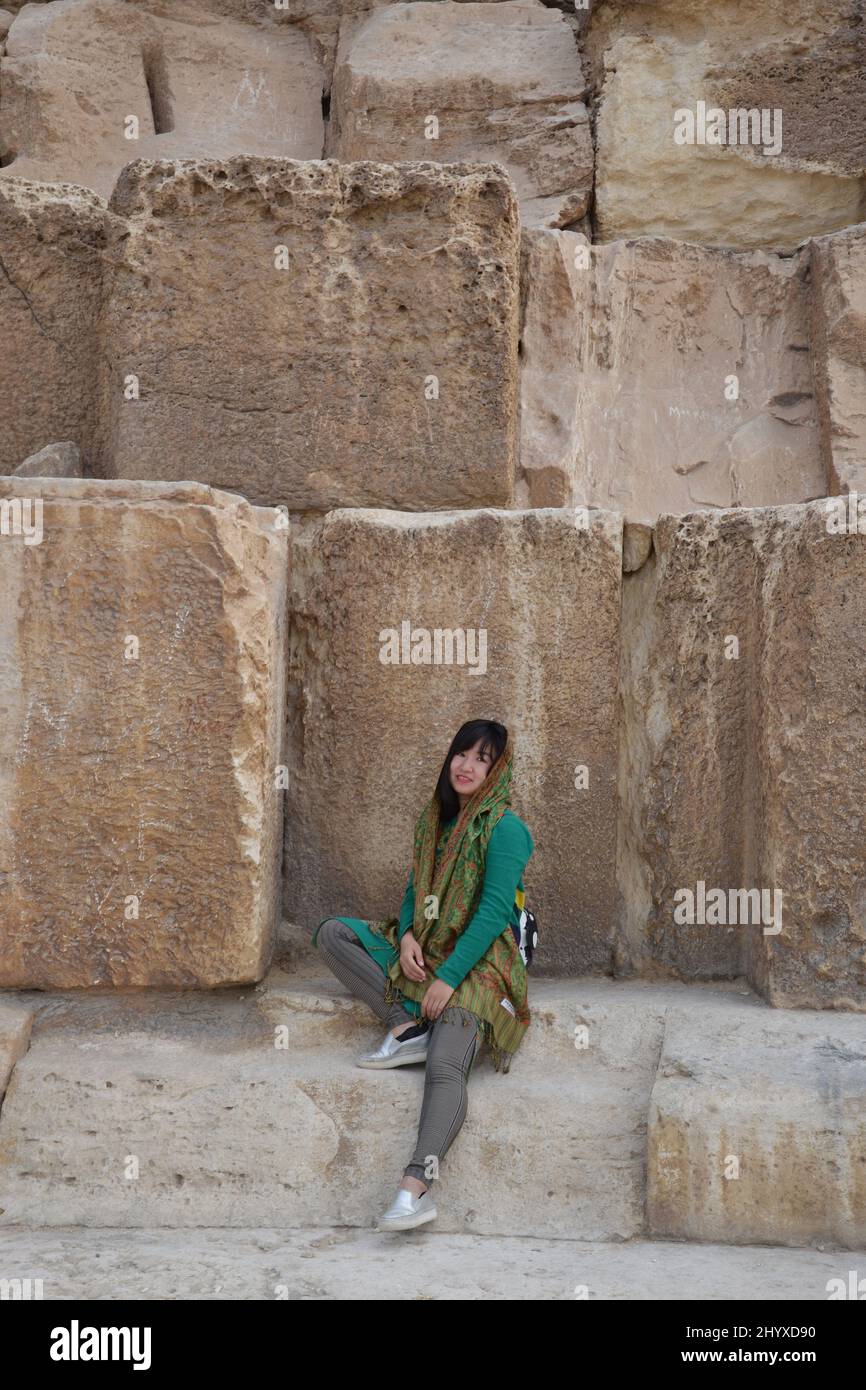 A vertical shot of a Chinese female sitting against the huge stones of ...