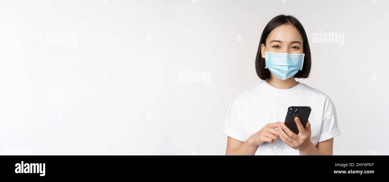 Health and covid-19 concept. Asian girl in medical face mask, using ...