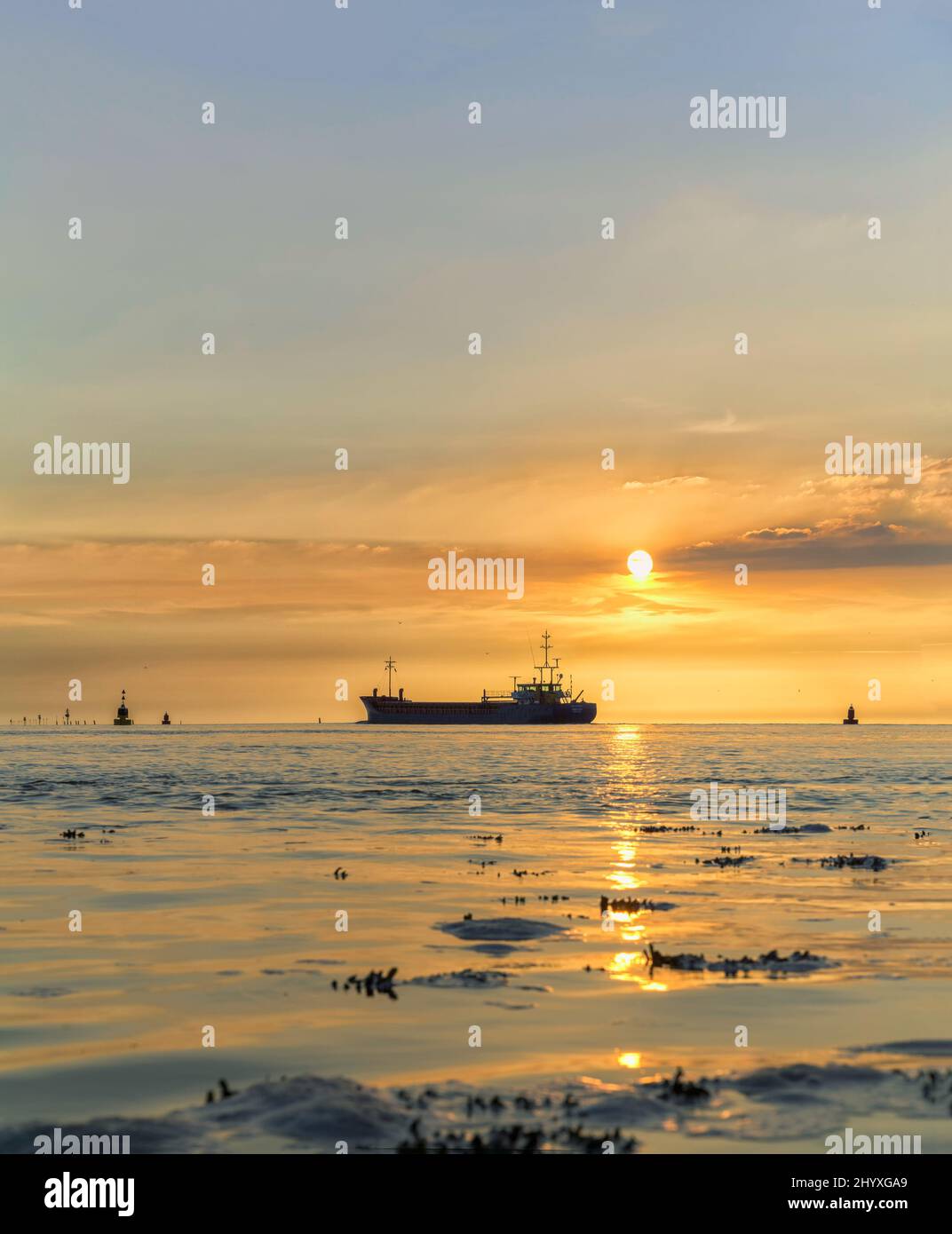 Golden sunset over the horizon on the ocean with a ship sailing by ...