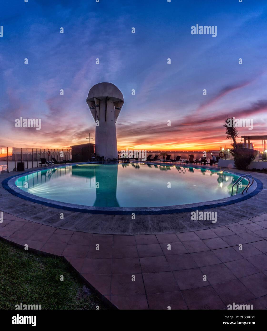 Wide-angle shot of a pool with a concrete tower next to it and a golden ...