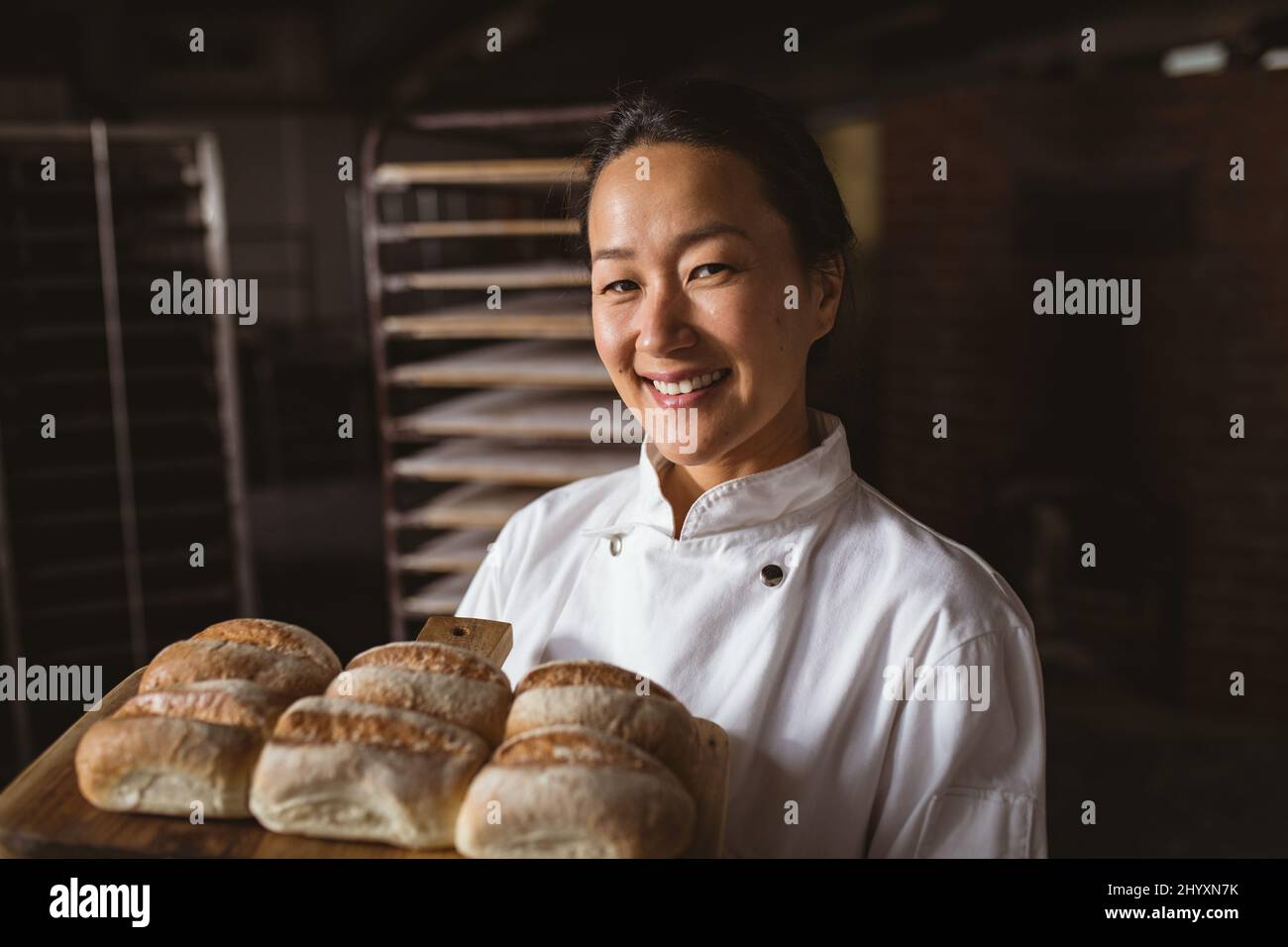 Portrait of smiling asian mid adult female baker showing fresh breads ...