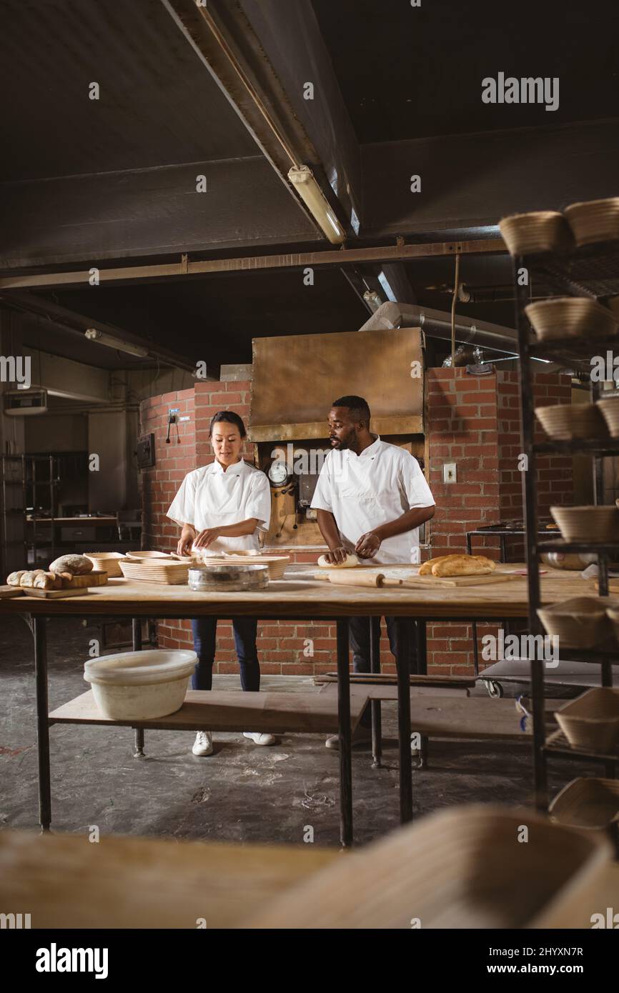 Multiracial male and female mid adult bakers talking while kneading ...