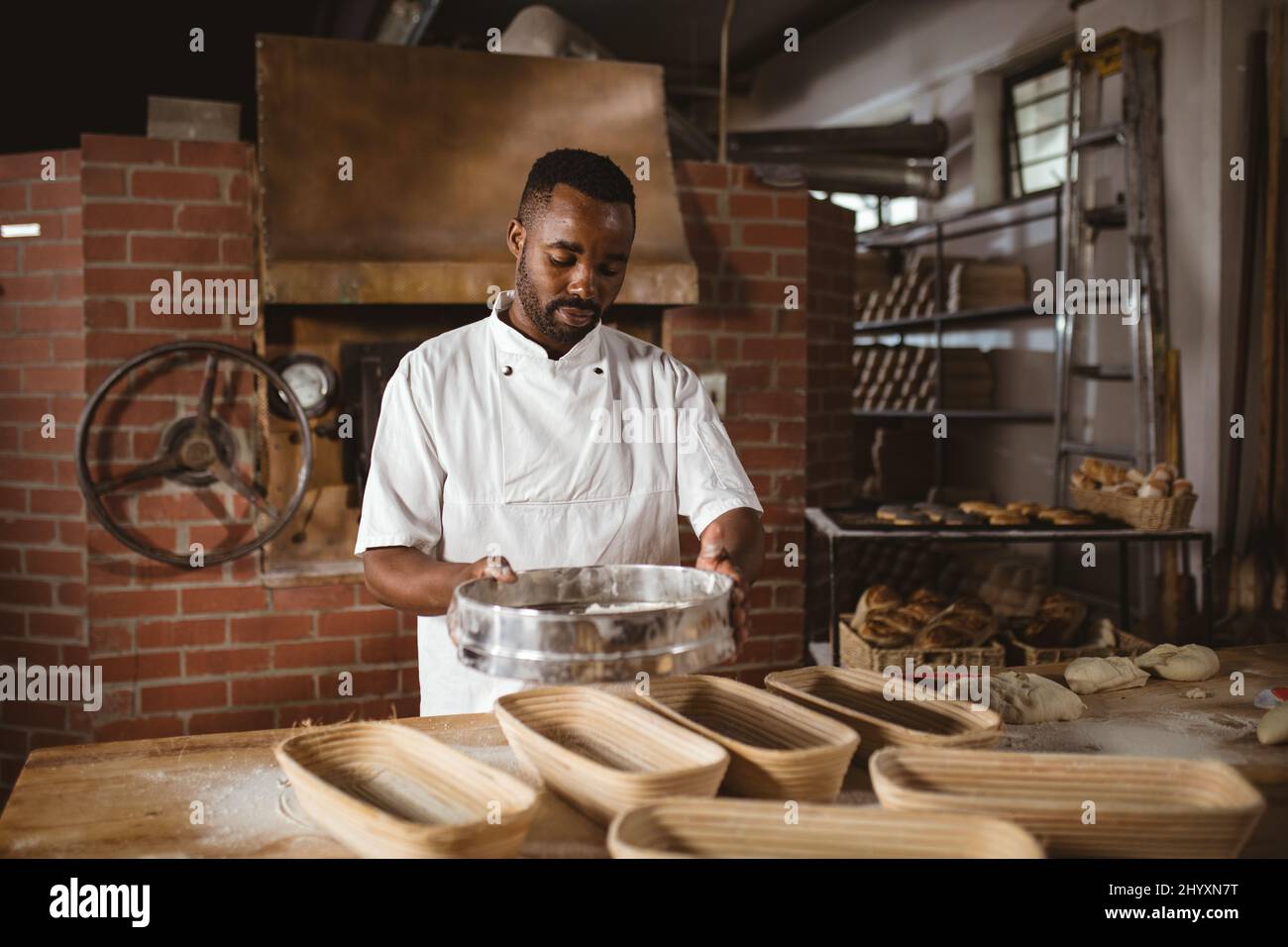 African american mid adult male baker straining flour over bread ...