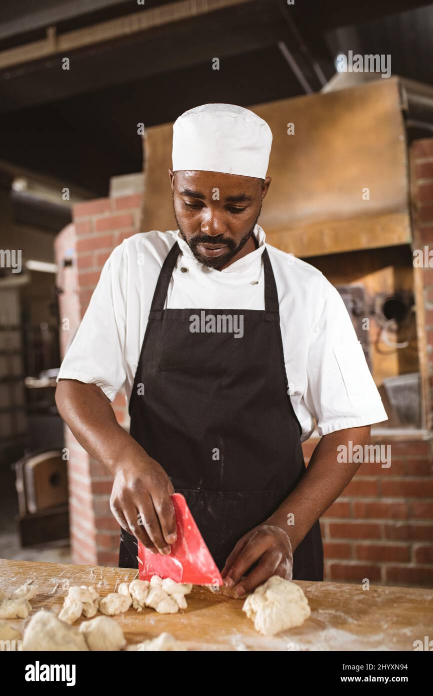 African american mid adult male baker cutting dough at table while ...