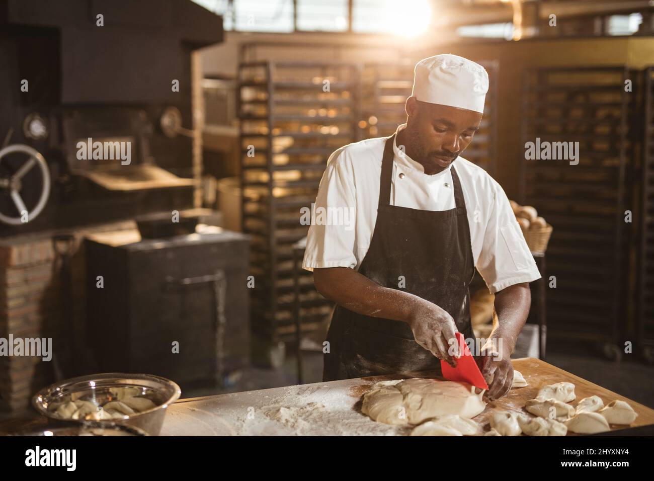 African american mid adult male baker cutting dough with dough cutter ...