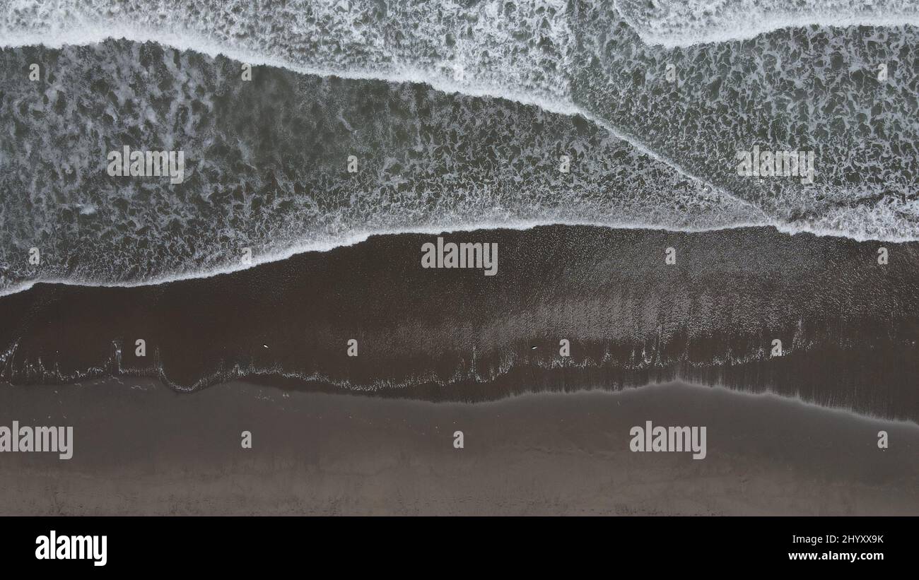An aerial view of the wavy sea hitting the sandy beach on the coast ...