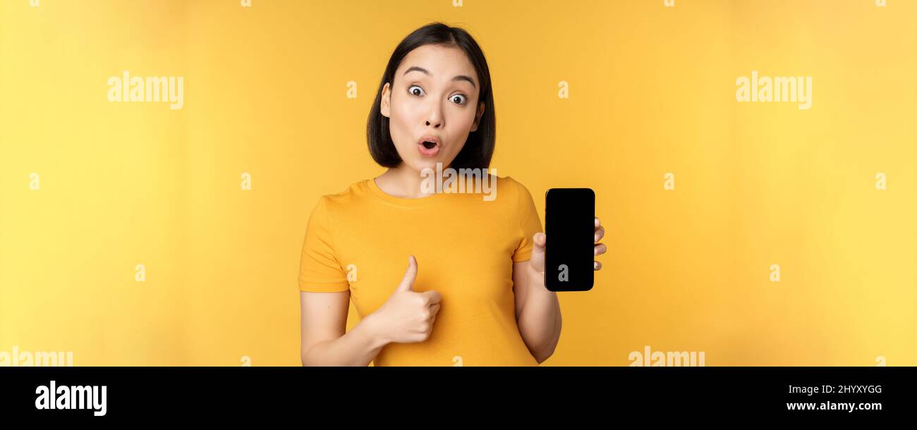 Excited asian woman showing mobile phone screen, thumbs up, like smth ...