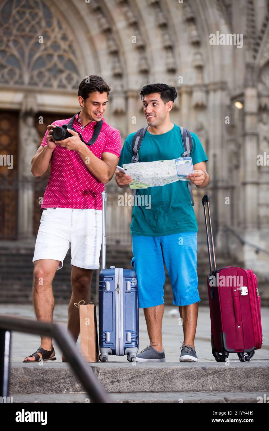 Two male tourists are walking with map and suitcases and photogr Stock ...
