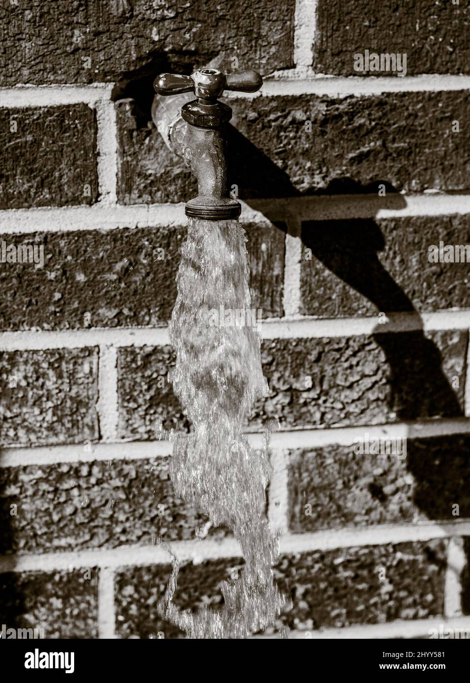 A vertical closeup of water streaming from a iron faucet on a brick ...