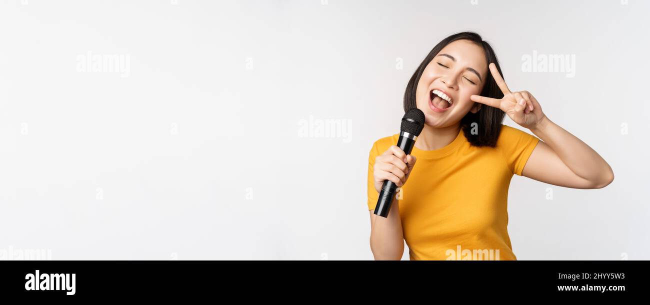 Happy asian girl dancing and singing karaoke, holding microphone in ...