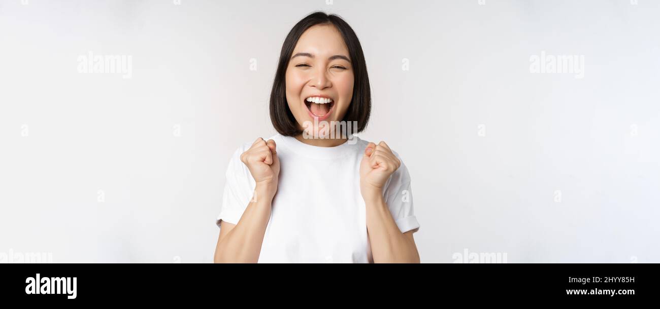 Portrait of enthusiastic asian woman winning, celebrating and ...