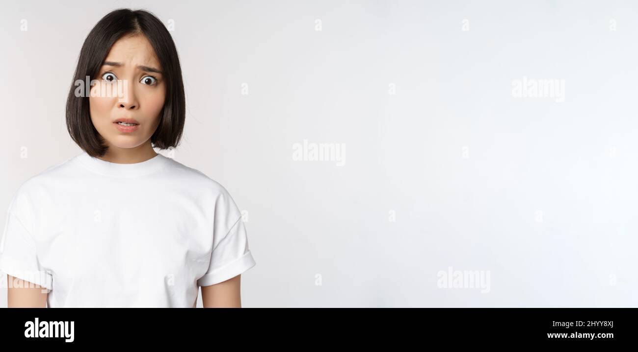 Image of shocked and frustrated asian woman, looking alarmed at camera ...
