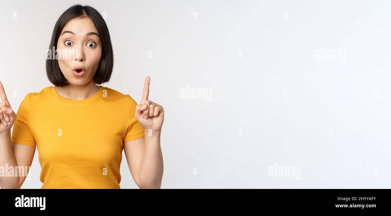 Portrait of impressed asian girl, pointing fingers up, say wow, looking ...