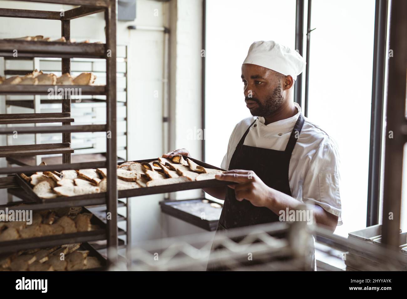 African american mid adult male baker removing baked bread tray from ...