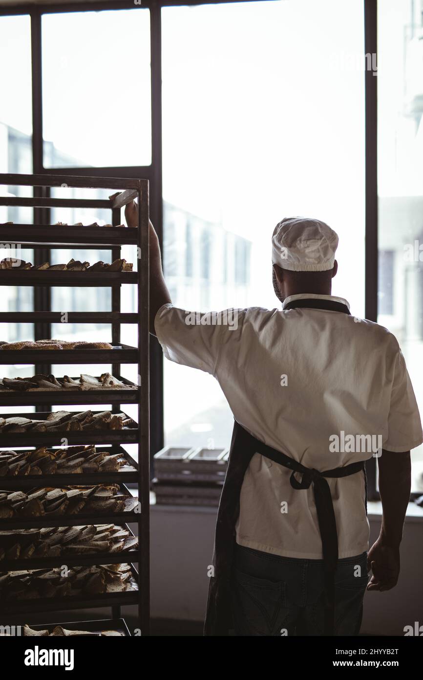 Rear view of african american mid adult male baker standing by rack by ...