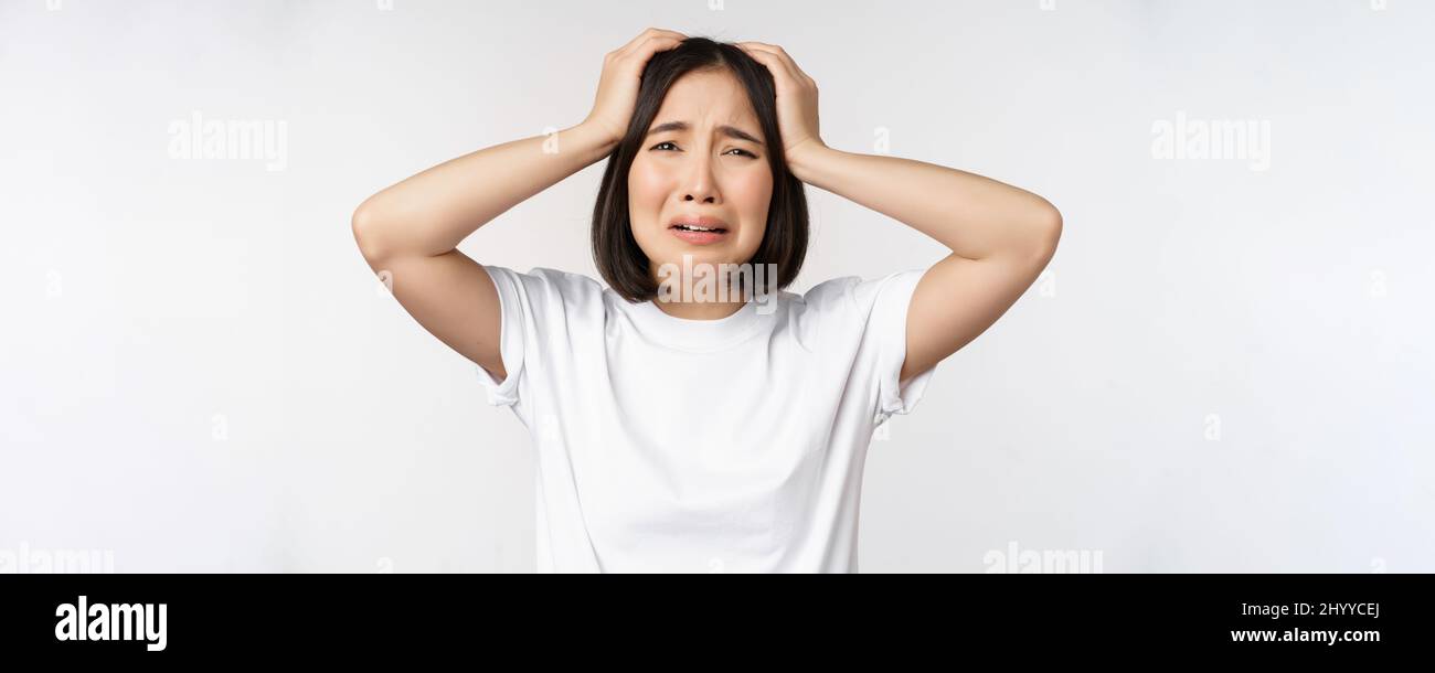 Desperate young korean woman holding hands on head, panicking, crying ...
