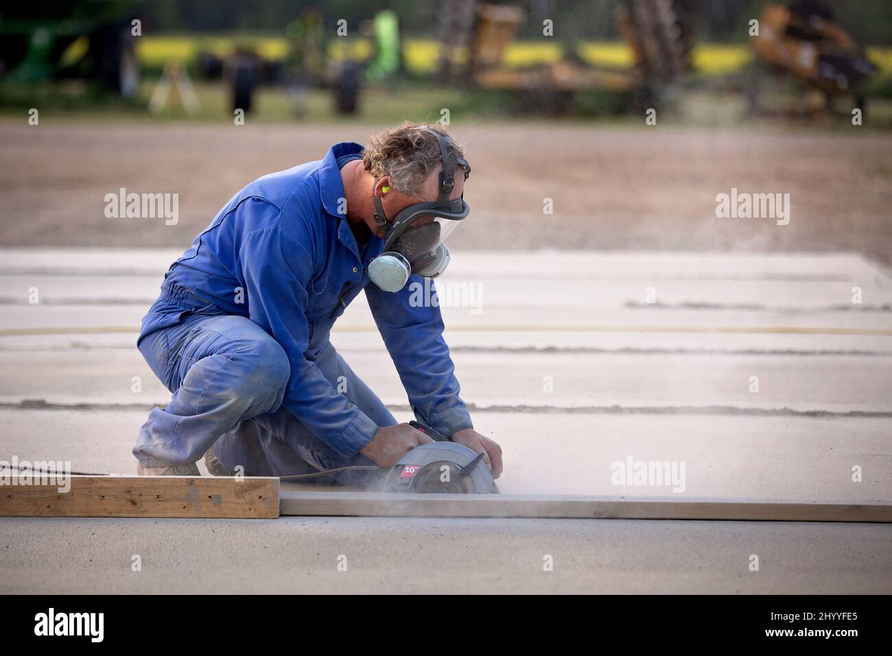 A man wearing a face mask cutting through concrete with a circular saw ...