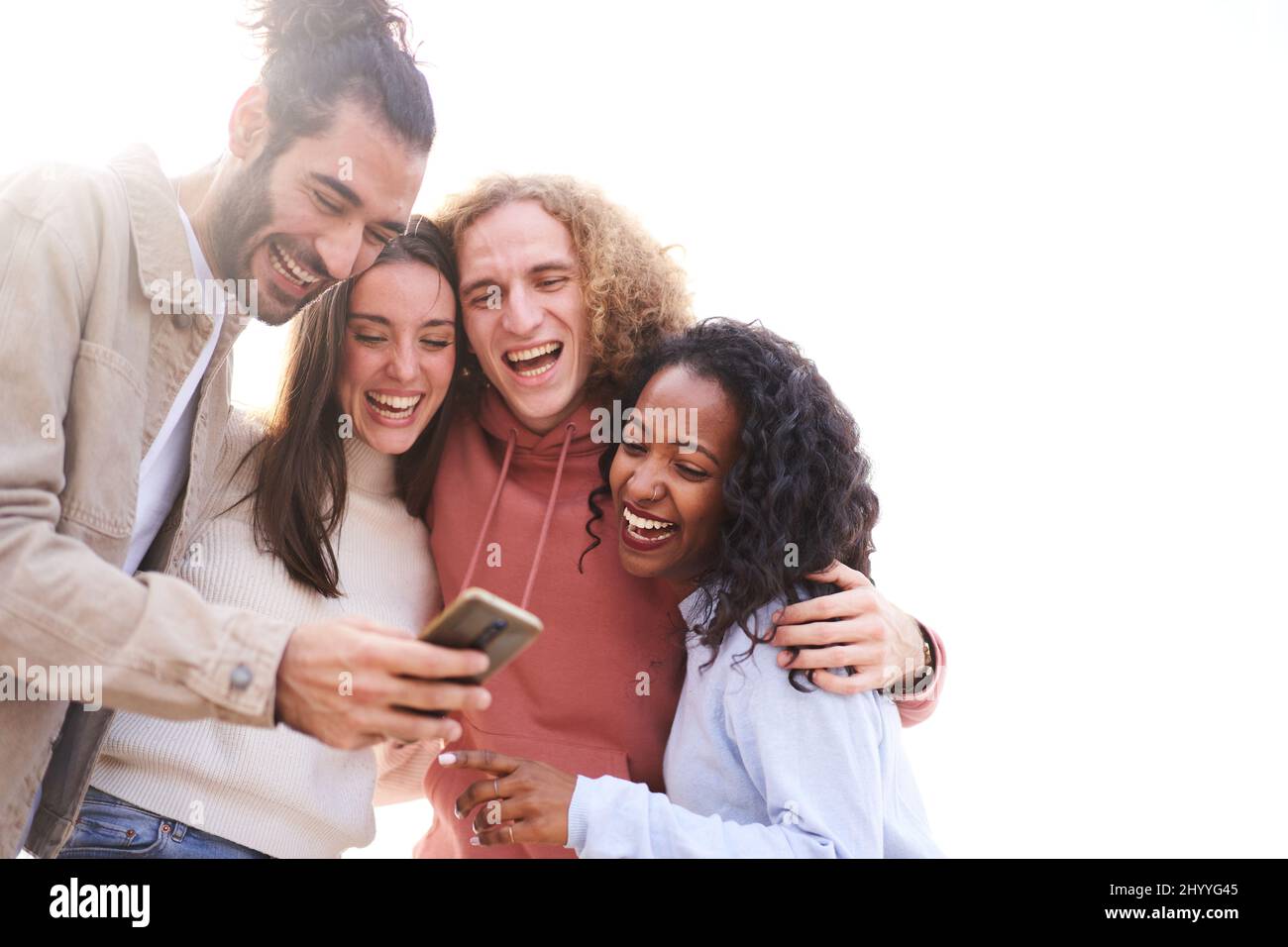 Four cheerful friends watching smartphone outdoors. People using ...