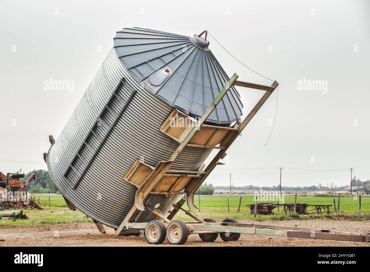 A steel grain bin tipped on a grain bin mover in a summer countryside ...