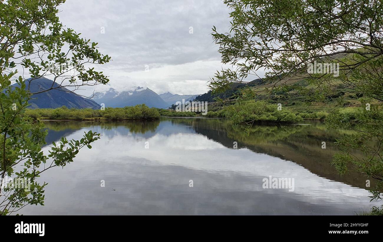 Body of water reflecting a mountain and plants under a bright sunlight ...