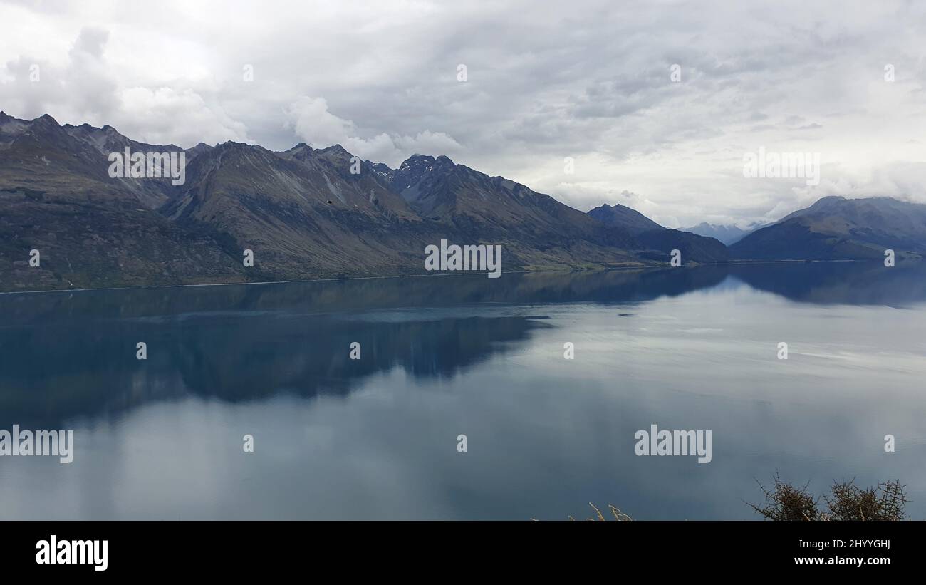 Body of water reflecting a mountain with a cloudy sky in the background ...