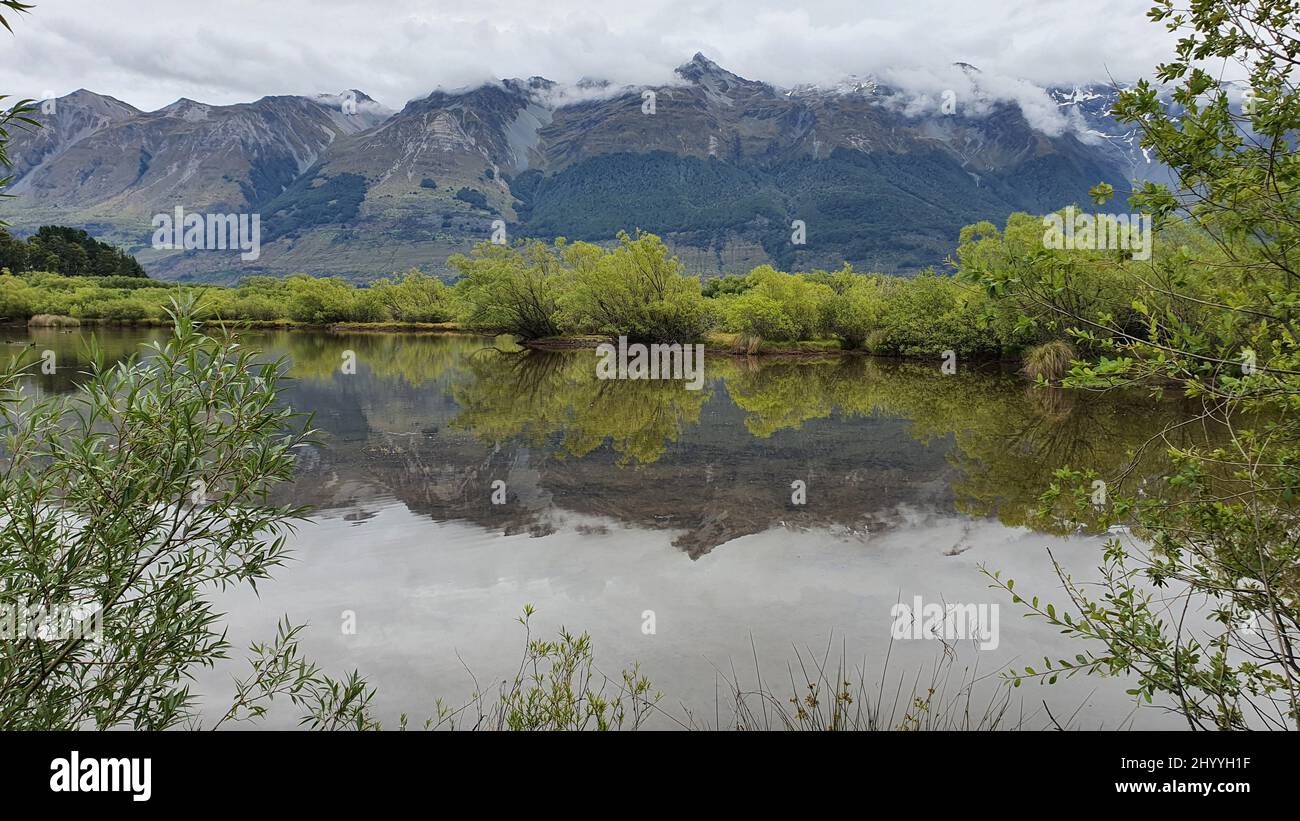 Body of water reflecting a mountain and plants under a bright sunlight ...