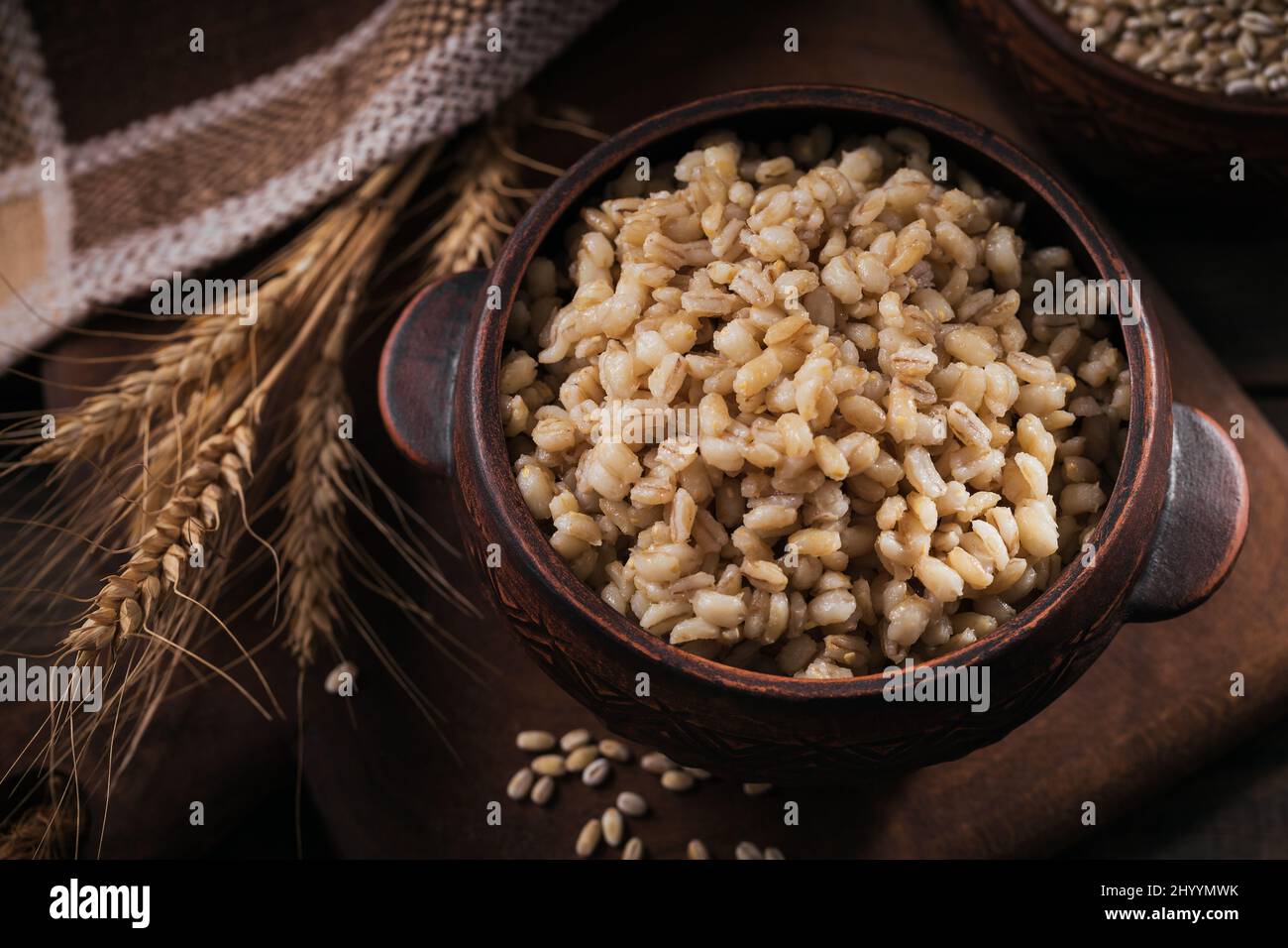 Bowl of cooked peeled barley grains porridge with ears of wheat on dark ...
