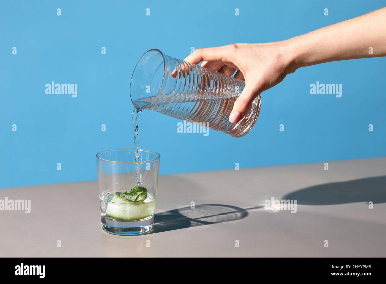 Minimal close up of female hand pouring water into glass against blue ...