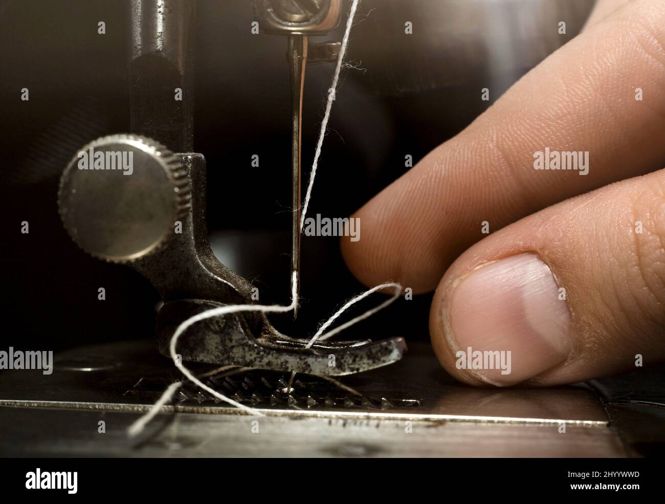 A hand threads a needle in an old retro sewing machine. Tools for the ...