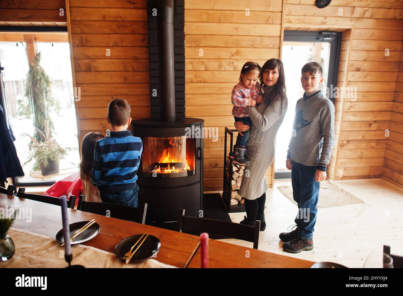 Mother and four kids in modern wooden house against table and fireplace ...
