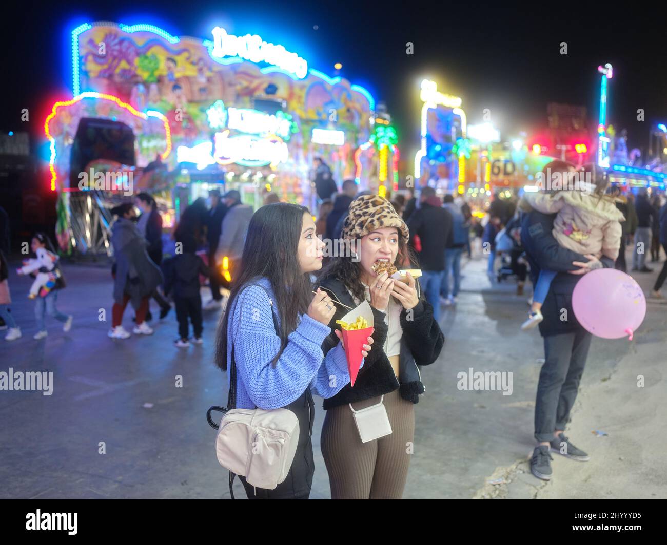 Women eating waffle and fries standing in the middle of a crowded night ...