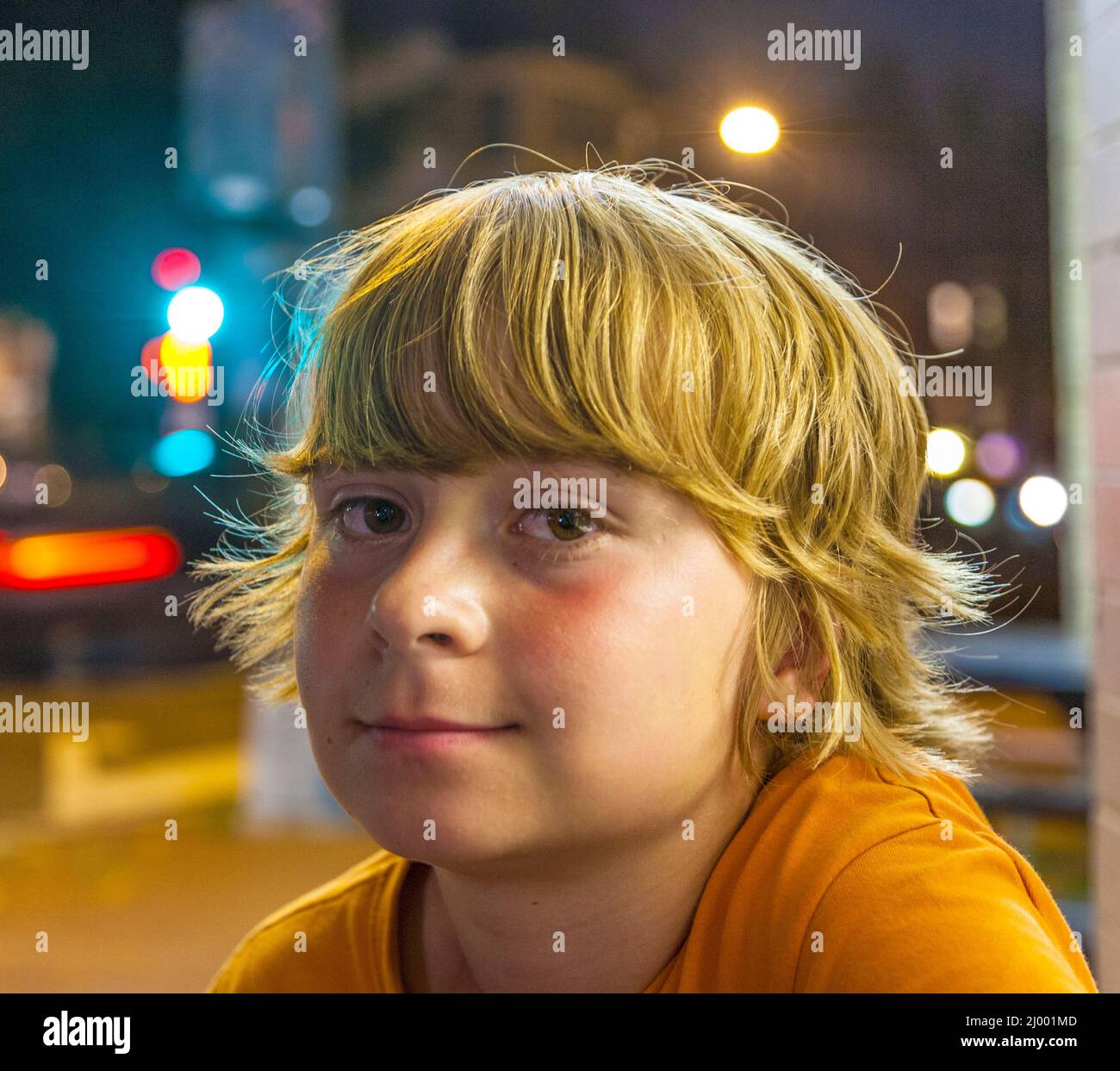 cute boy smiles tired while sitting outside by night next to the street ...