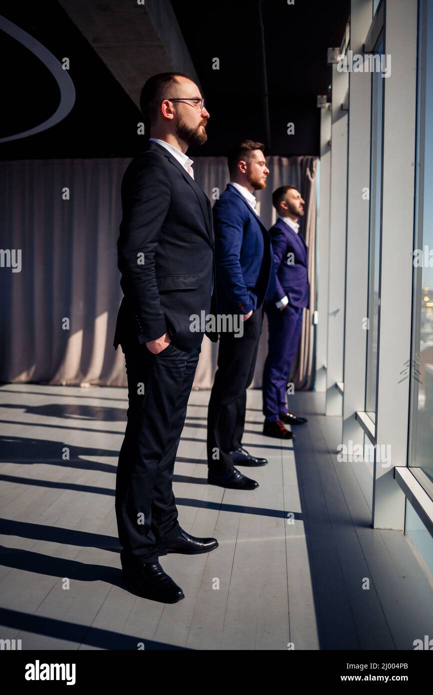Three successful businessmen stand in a row and look out the window ...