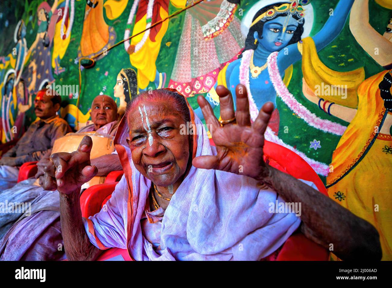 An elderly Indian widow covered with color powder poses for a photo ...