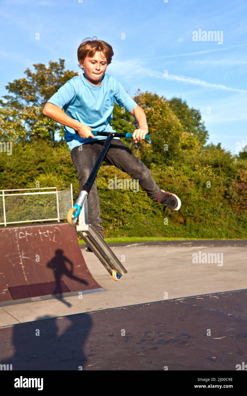 boy jumps with scooter at the skate park over a ramp and has fun Stock ...