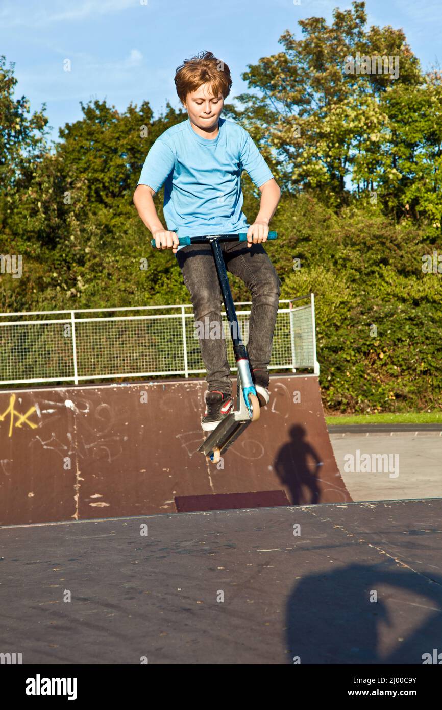boy jumps with scooter at the skate park over a ramp and has fun Stock ...